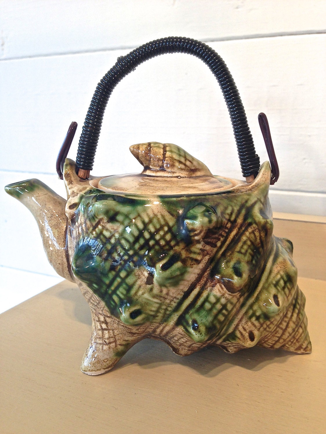 a really unusual tea pot in the shape of a shell, with a wire and cane ...