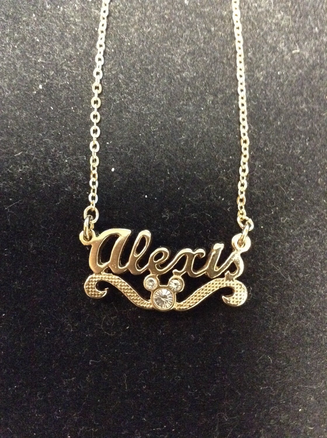 DISNEY Alexis name necklace in gold tone. Scroll work accented